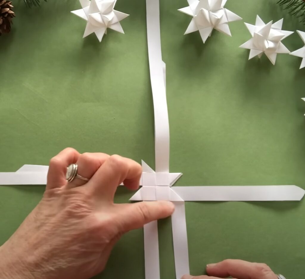 Woman folds up 4 thin strips of paper and weaves them together to make ...