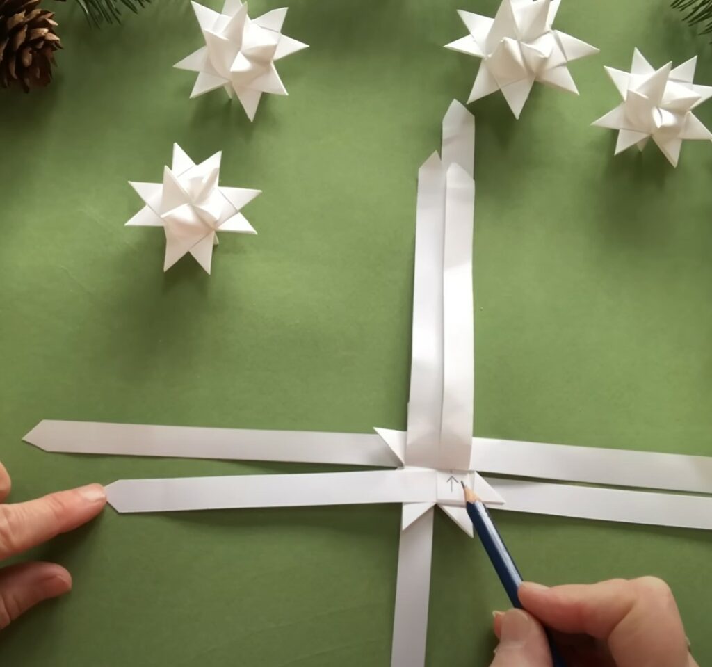 Woman folds up 4 thin strips of paper and weaves them together to make ...